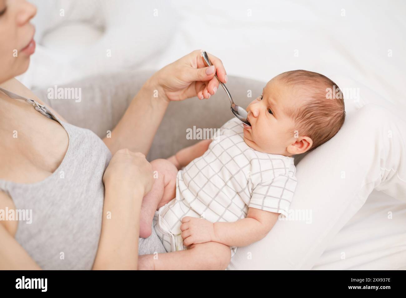 Mother feeding newborn baby with vitamin or liquid medicine using spoon ...