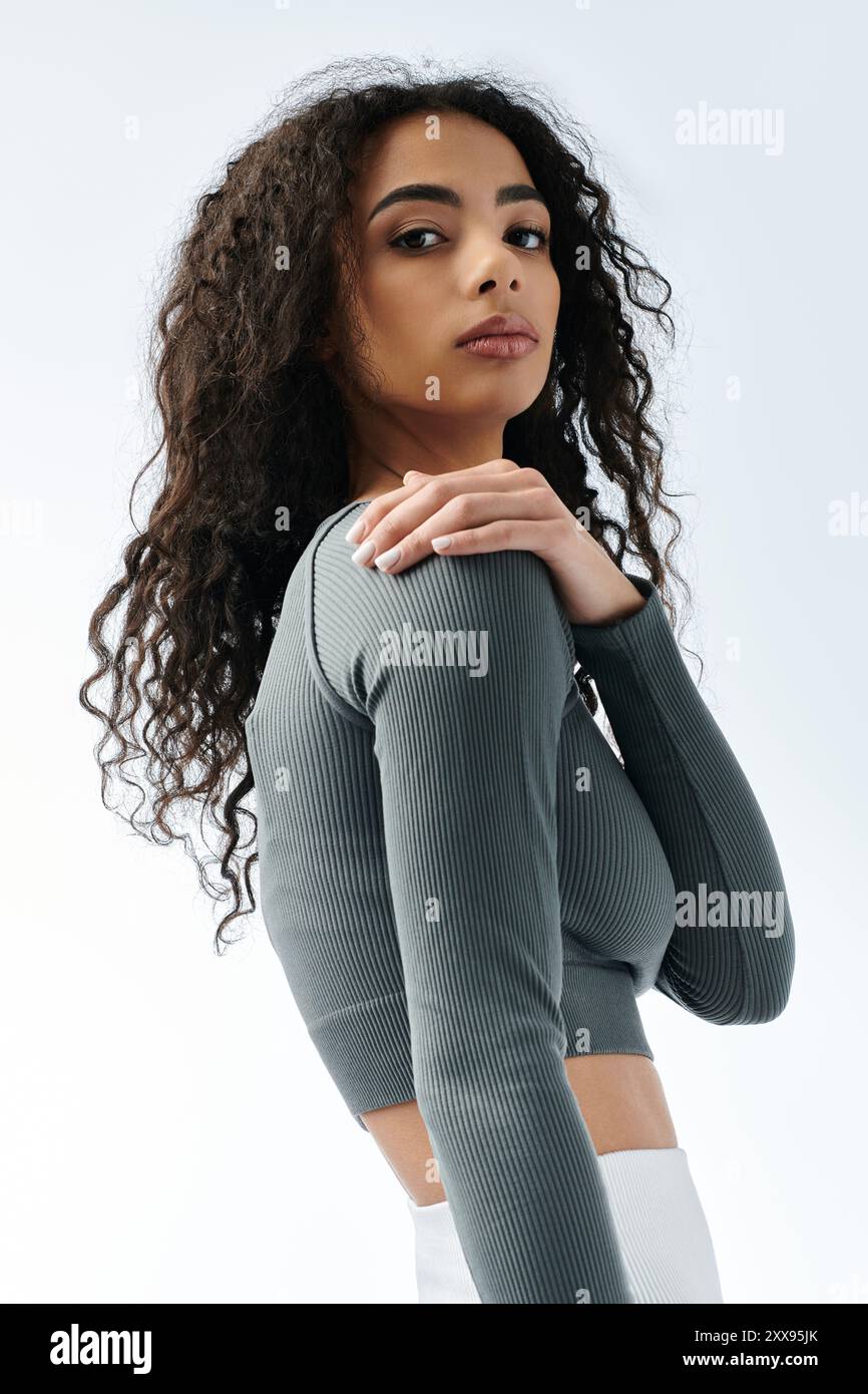 A young woman with curly hair poses confidently in a grey workout top ...