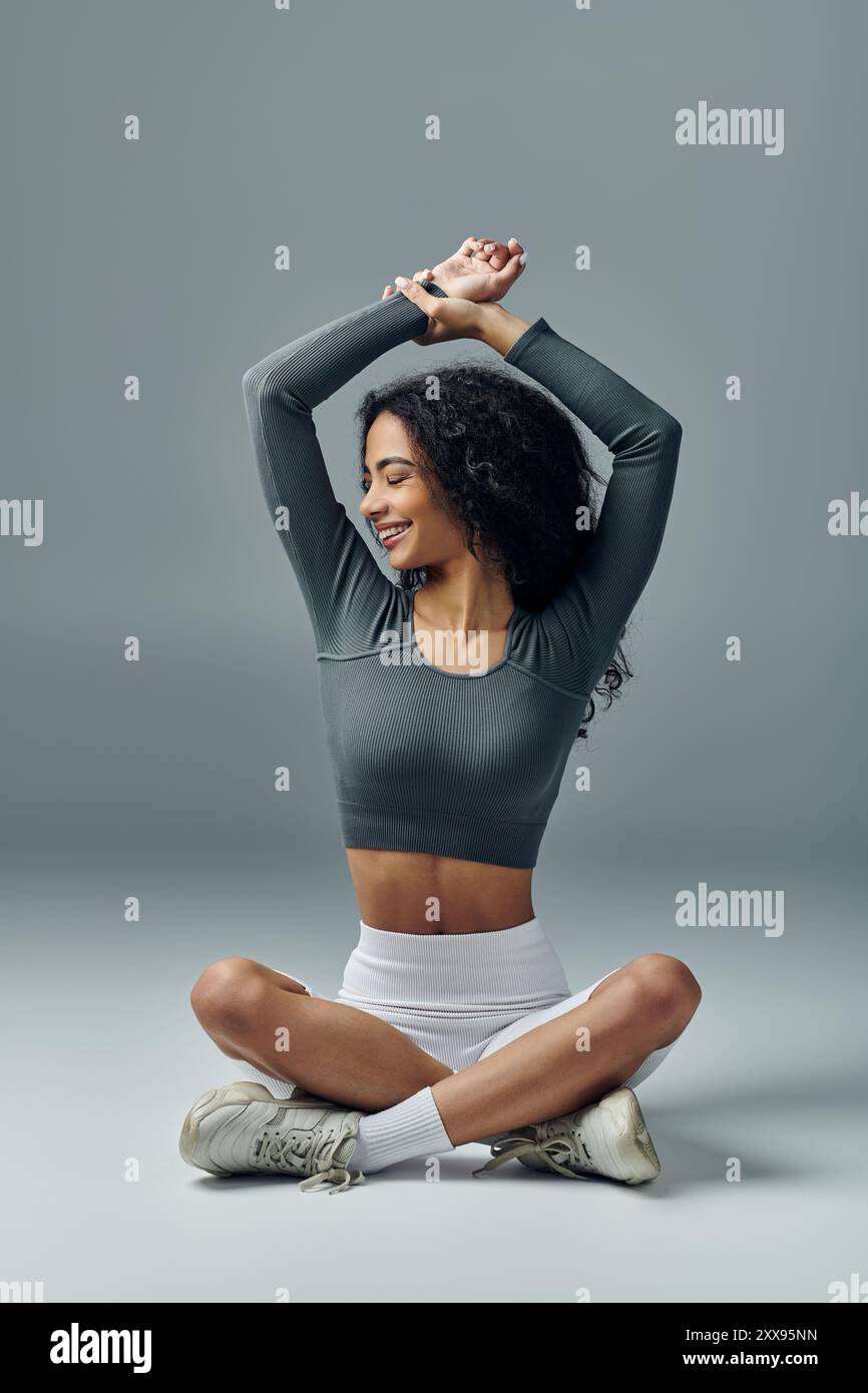 A young woman with curly hair sits cross-legged, stretching her arms ...