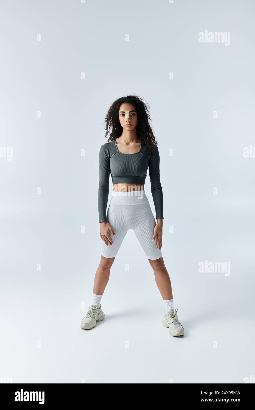 A young woman in athletic wear stands with her feet apart in a fitness ...