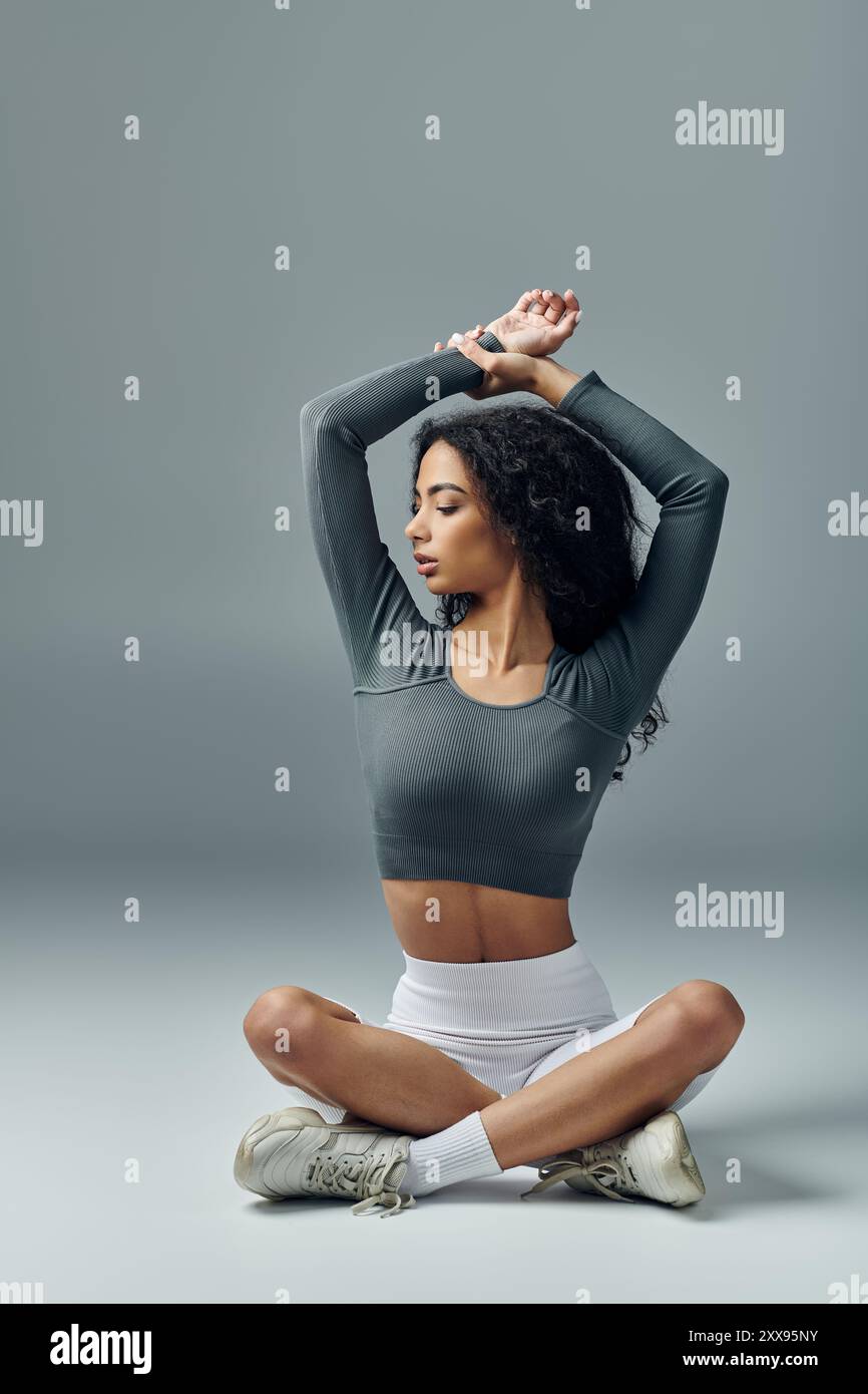 A young woman in athletic wear sits with her legs crossed on a grey ...