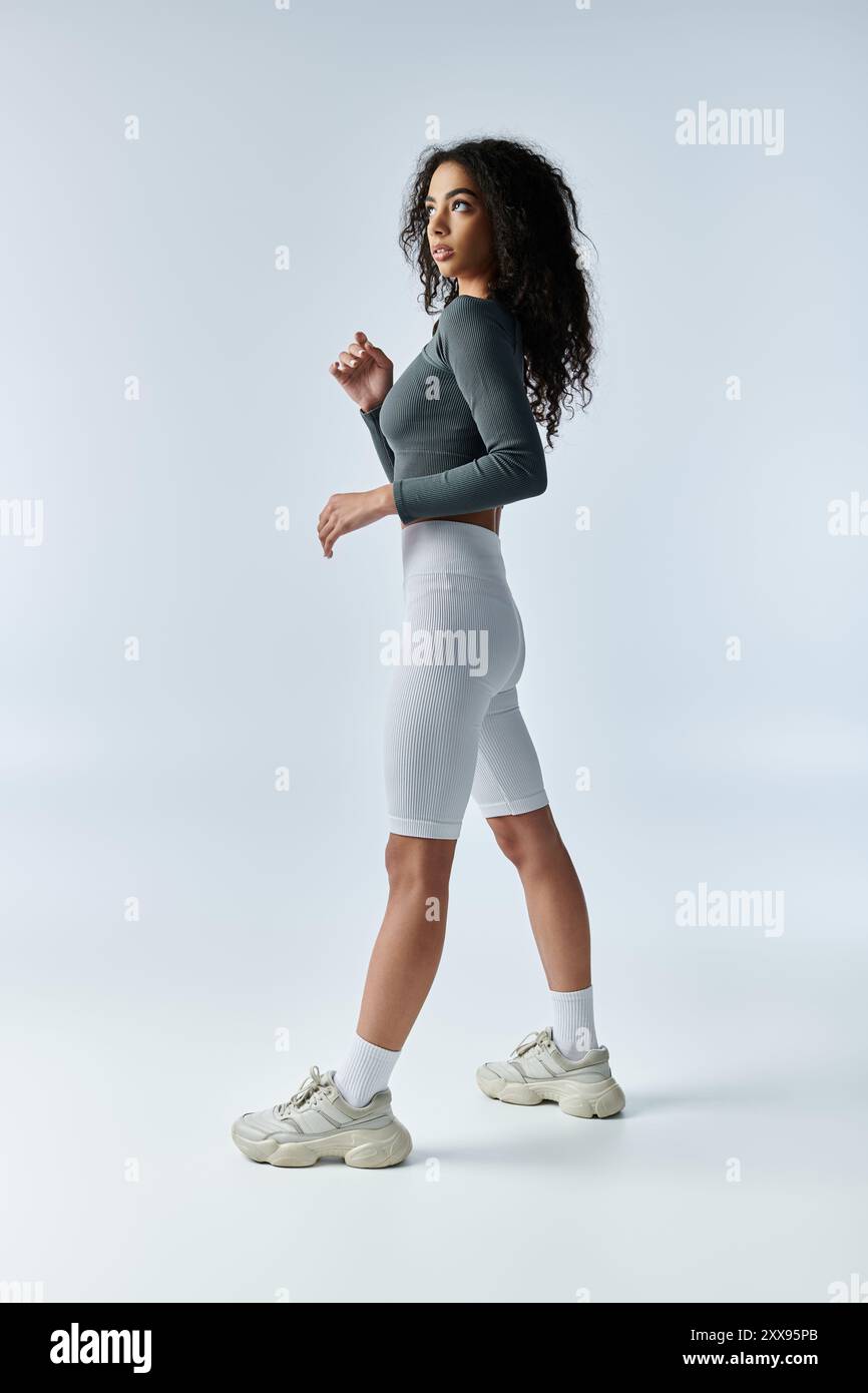A young woman, confidently strides across a white backdrop ...