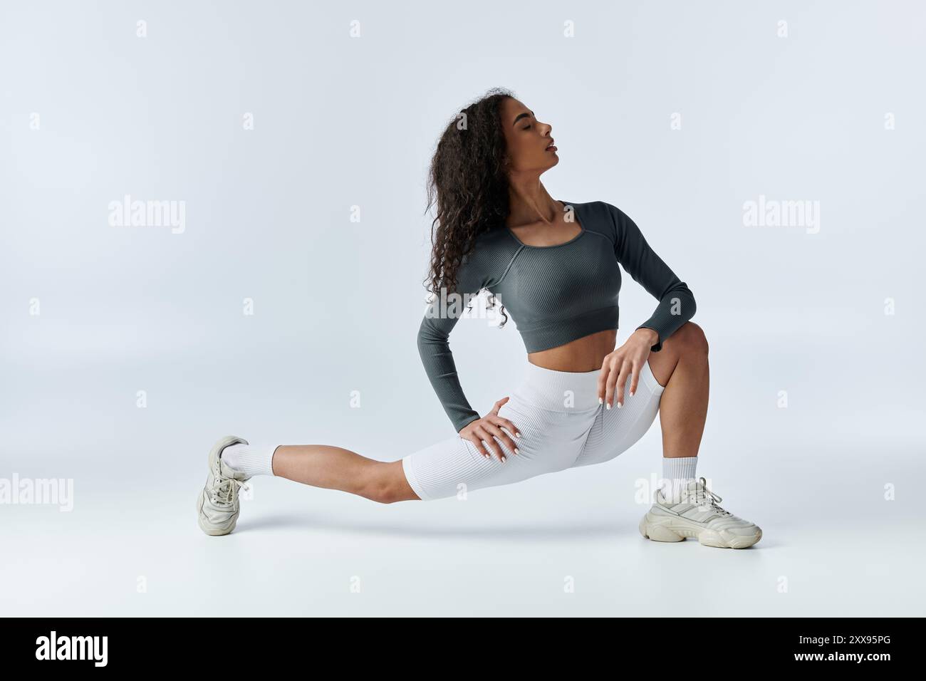 A young woman in a grey top and white shorts performs a stretching ...