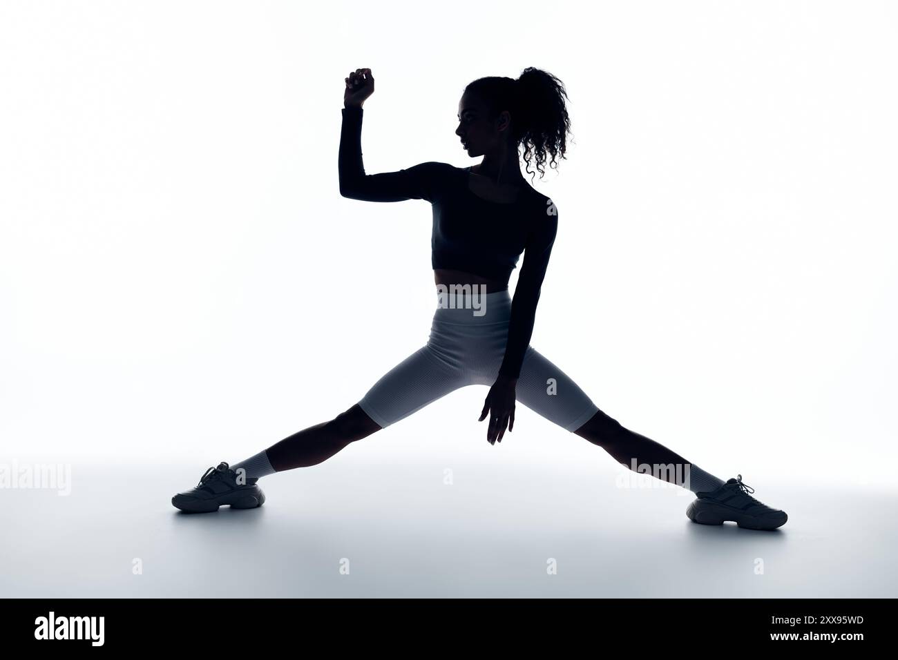 A young woman with a ponytail stretches her leg out in a studio with a ...
