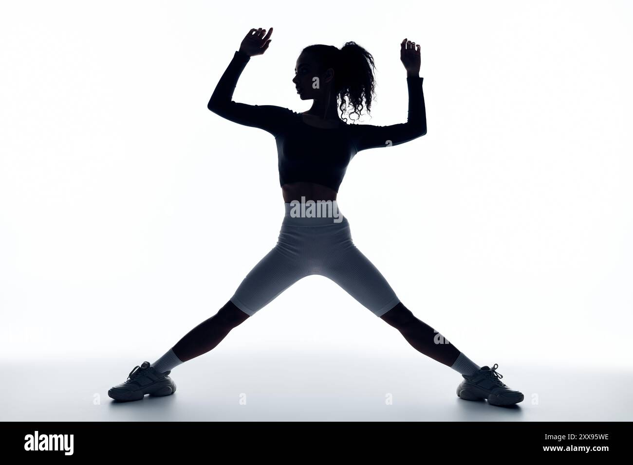 A young Black woman in athletic wear stretches her legs and arms in a ...