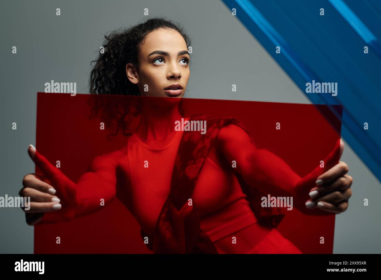 A young African American woman poses with a red glass pane in a studio ...