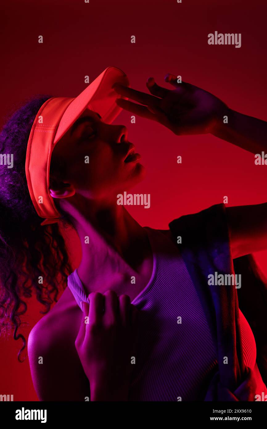 A young woman with curly hair, wearing a visor, poses dramatically in a ...