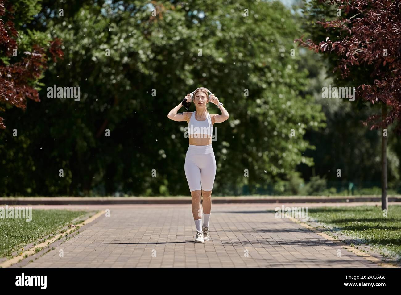 A young woman with vitiligo in white activewear walks on a paved path ...