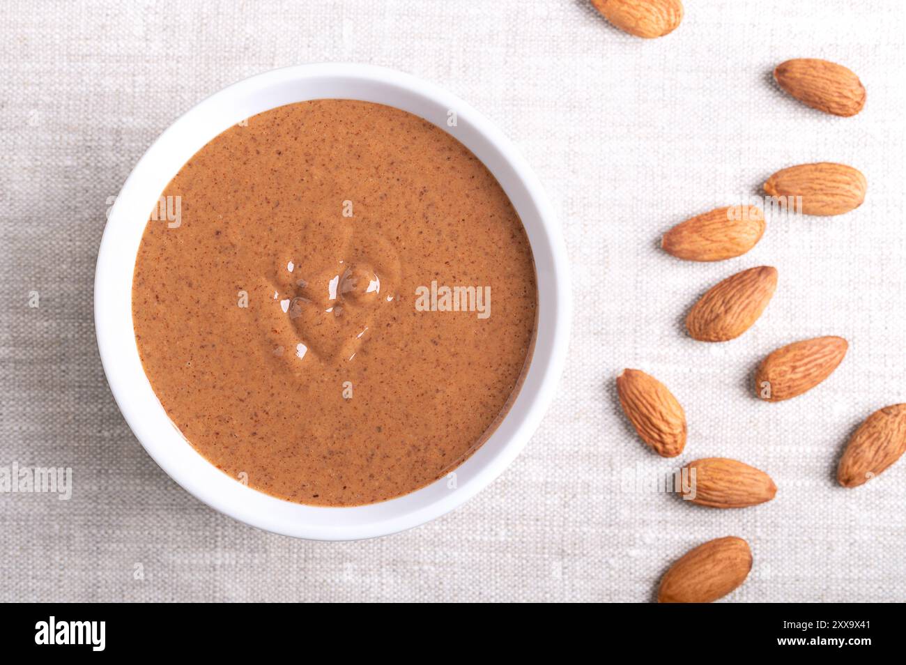 Almond butter in a white bowl on linen fabric. Brown and smooth food ...