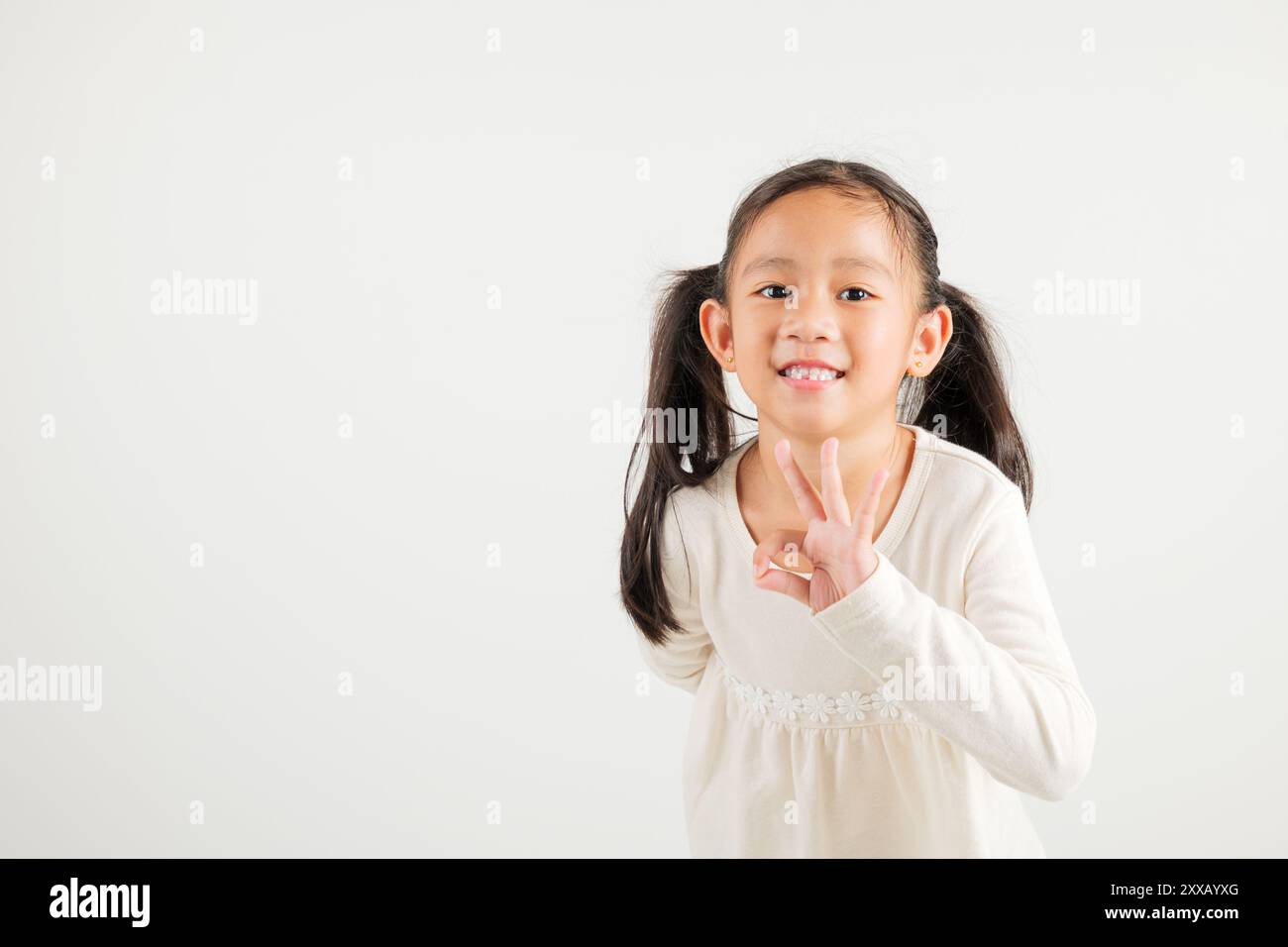 Exuberant young kid girl showcases the OK sign with an optimistic smile ...