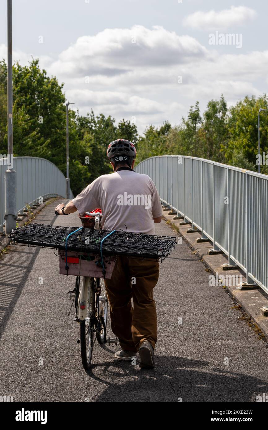 Man wearing a helmet is pushing his bicycle with birdcages strapped to ...