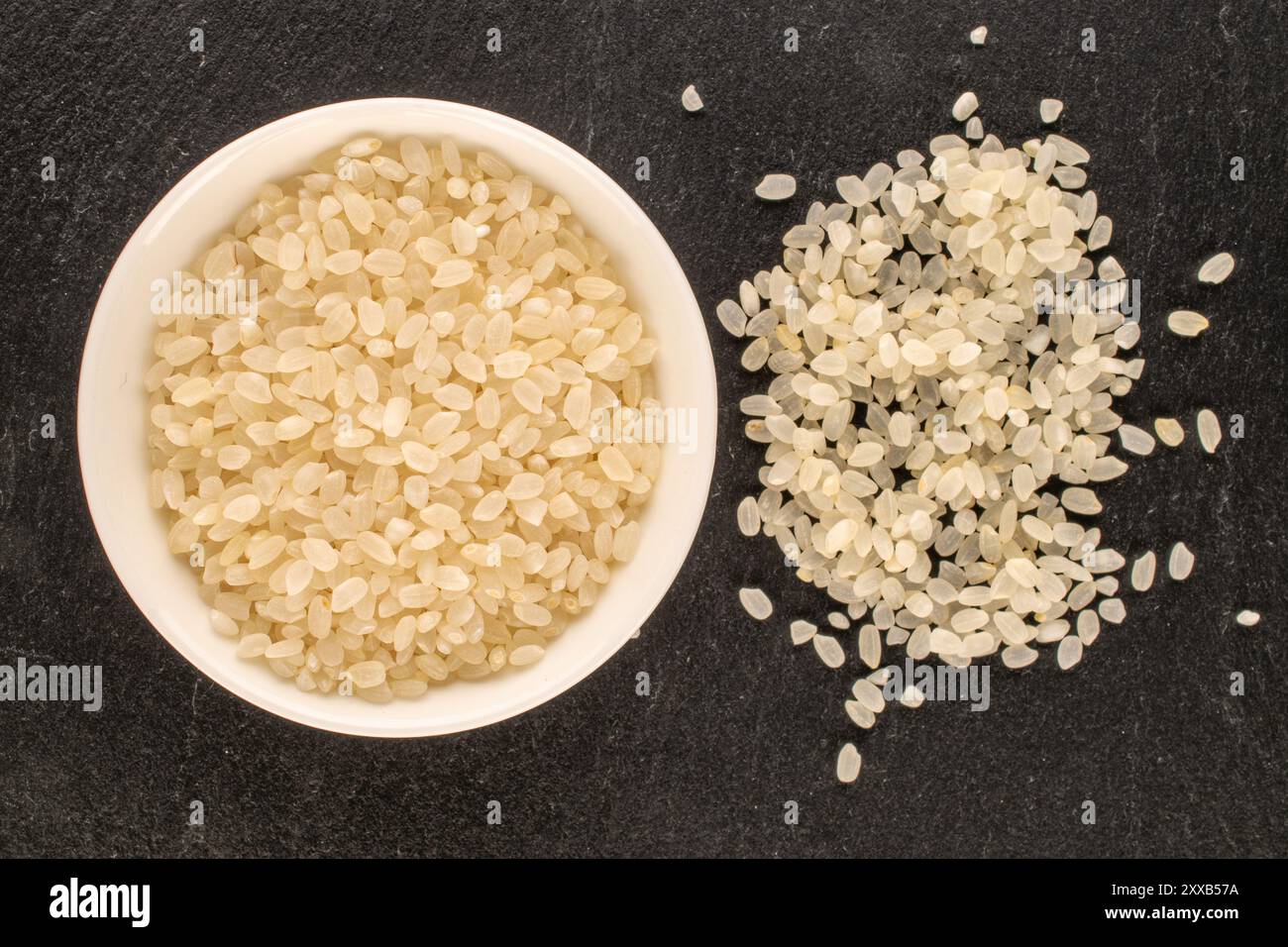 Round grain uncooked rice with white ceramic saucer on slate stone ...