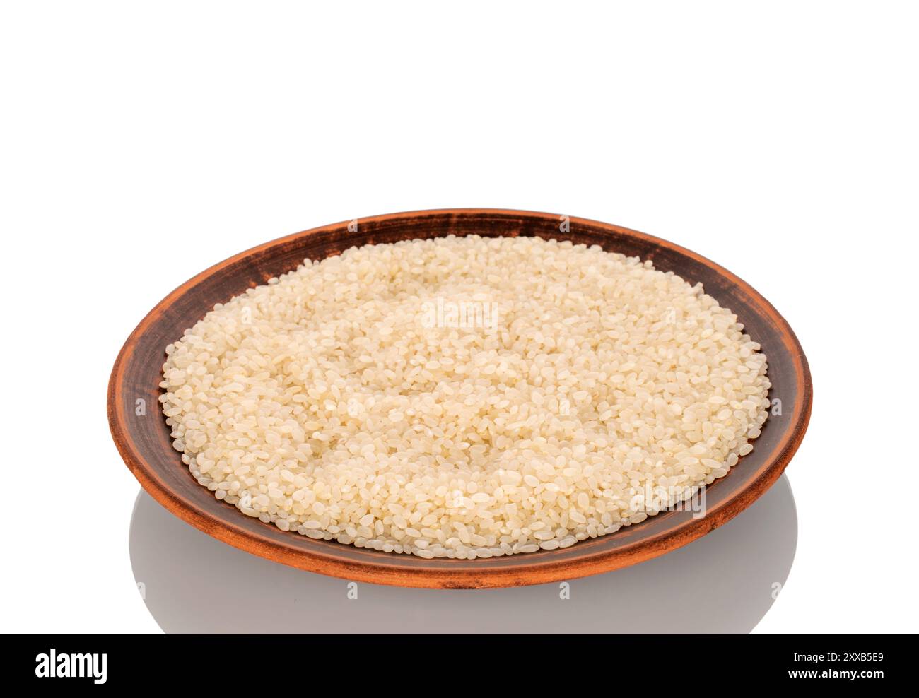 Round grain uncooked rice in a clay plate, macro, isolated on white ...