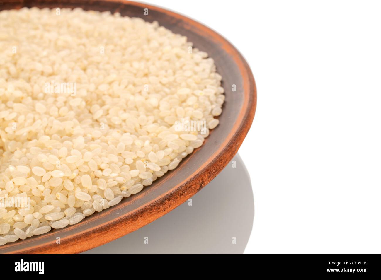 Round grain uncooked rice in a clay plate, macro, isolated on white ...