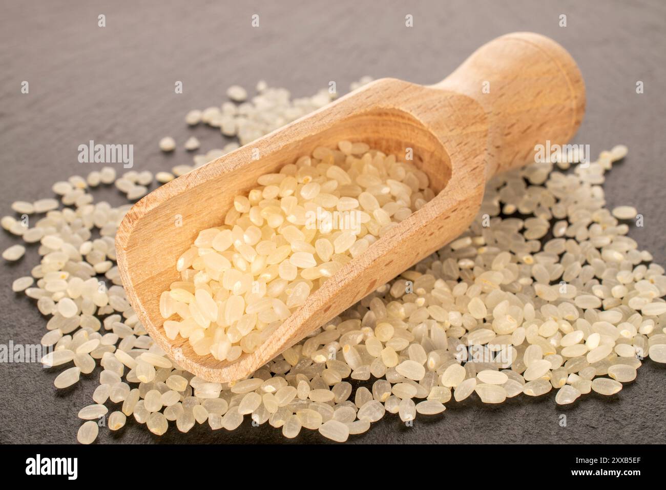 Round grain uncooked rice with wooden spoon on slate stone, macro Stock ...