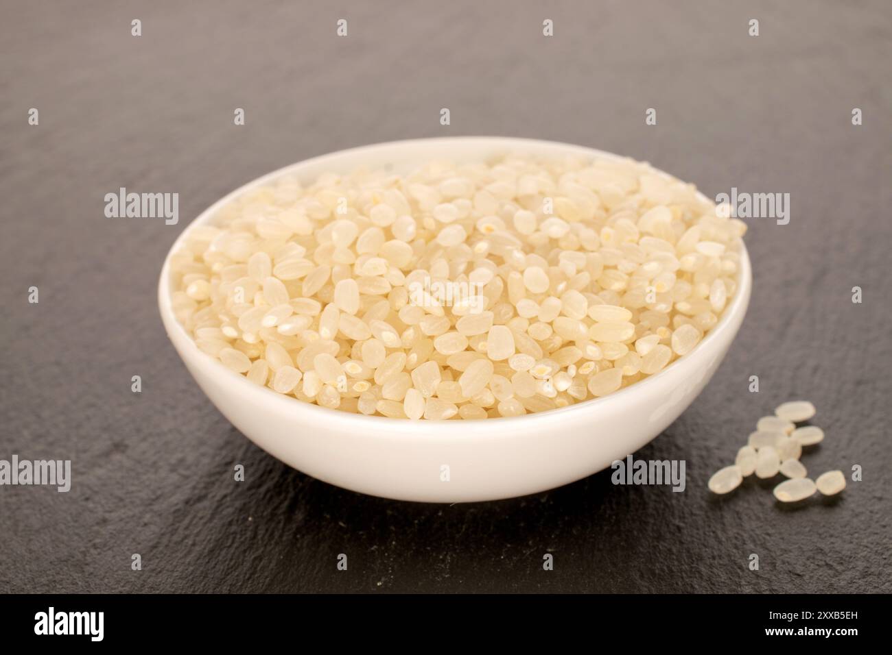 Round grain uncooked rice with white ceramic saucer on slate stone ...
