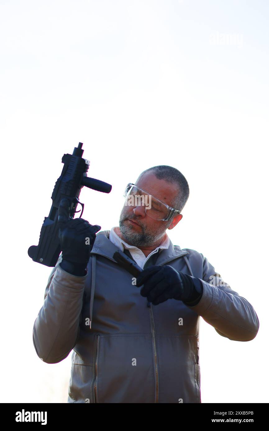 Man with gray jacket shooting black rifle aims at the target on a white ...