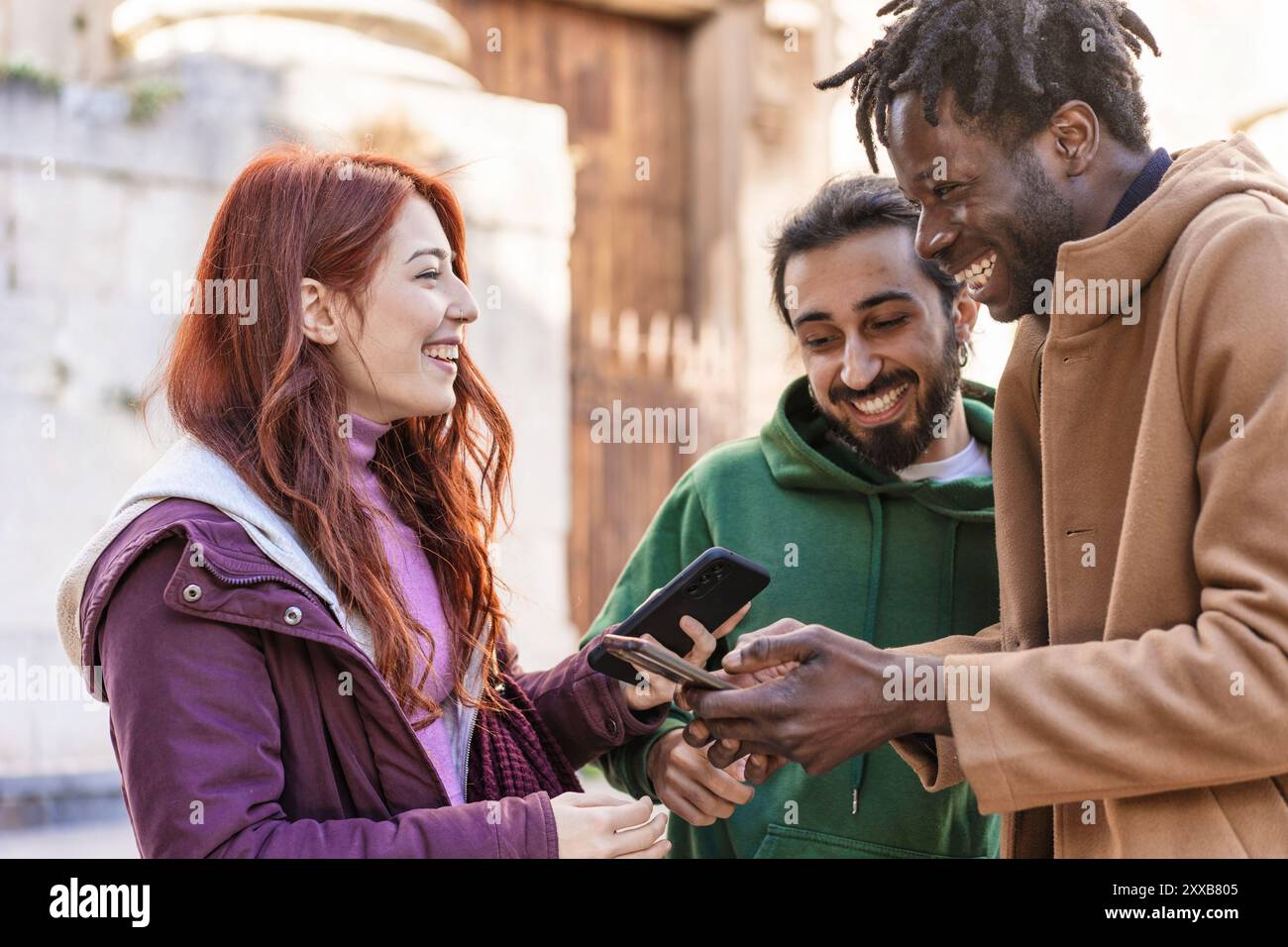 Cheerful multicultural friends looking at smartphone together in urban ...