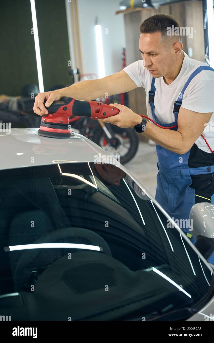 Worker uses a modern polishing machine during the detailing process ...