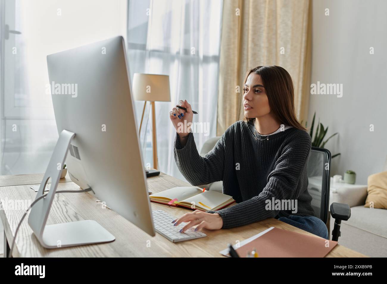A young woman sits at her desk, working on her computer, focused on her ...