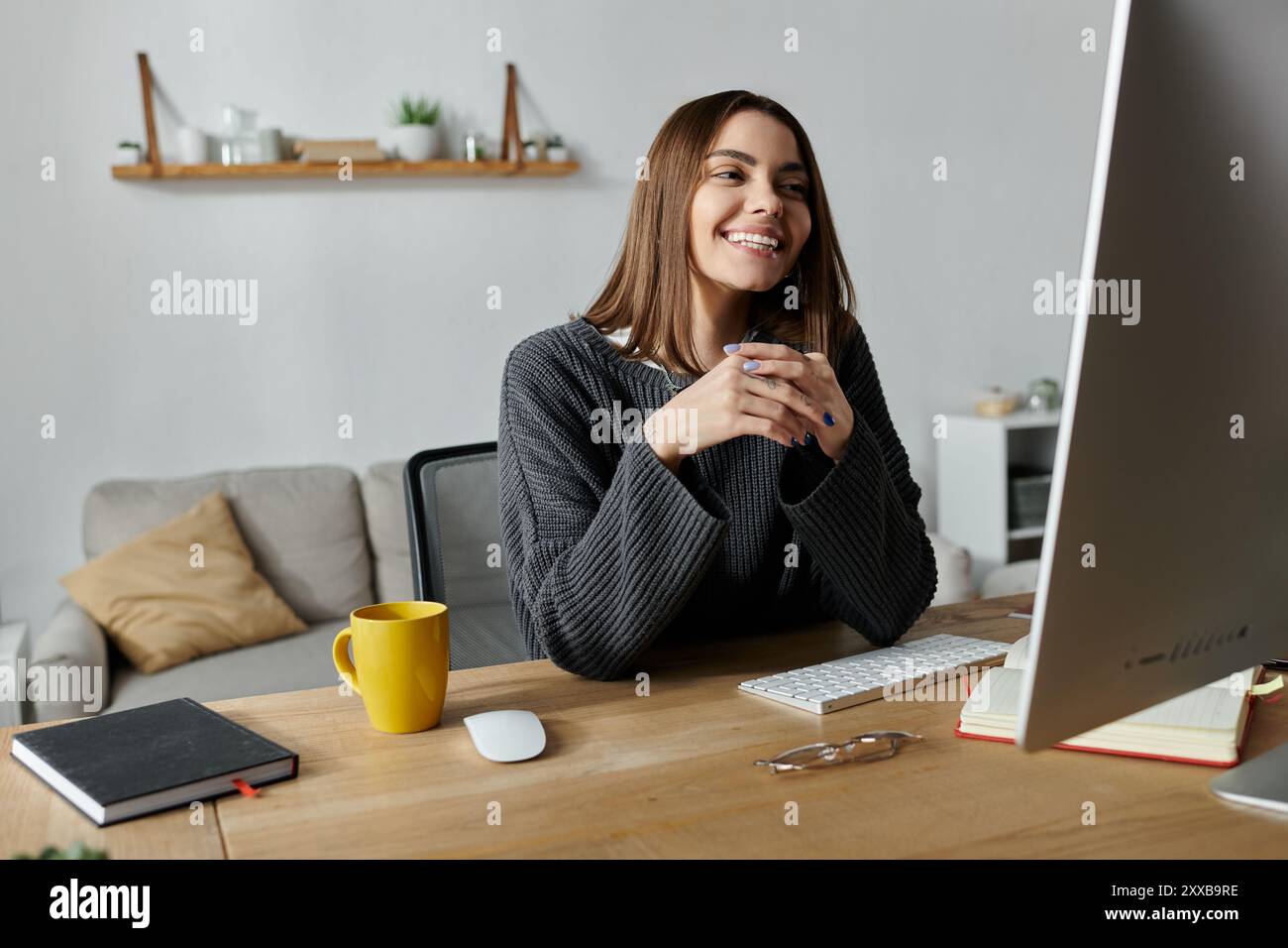A young woman smiles brightly as she works on her computer in her home ...