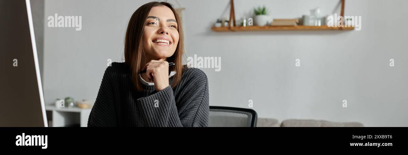 A young woman in a grey sweater sits at her desk, smiling and looking ...