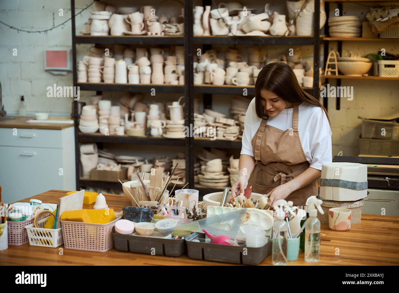 Young woman in apron showing process of creating pottery Stock Photo ...