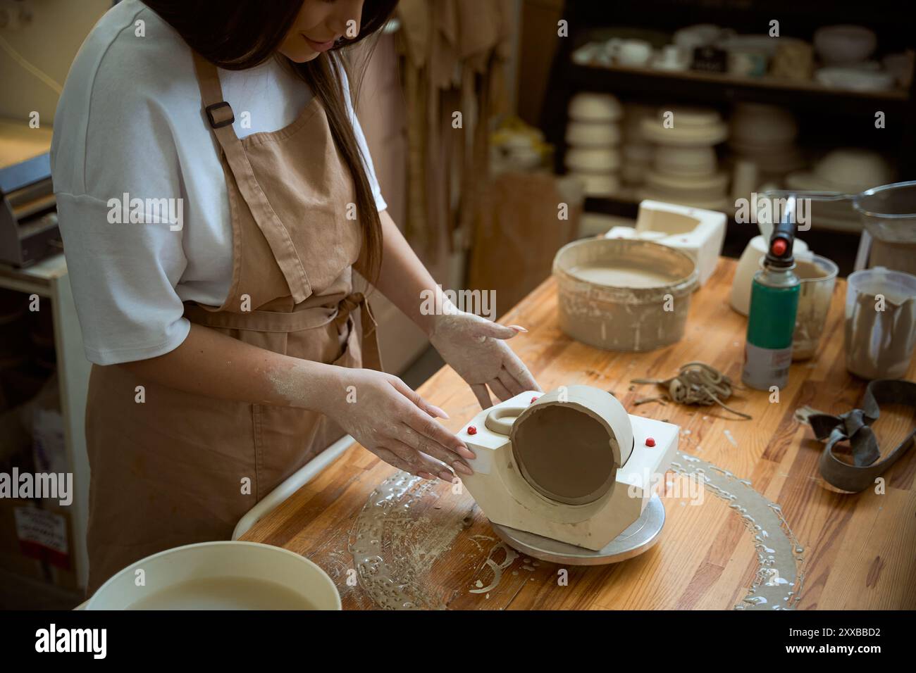 Table in pottery studio with female artist shaping wet clay for potter ...