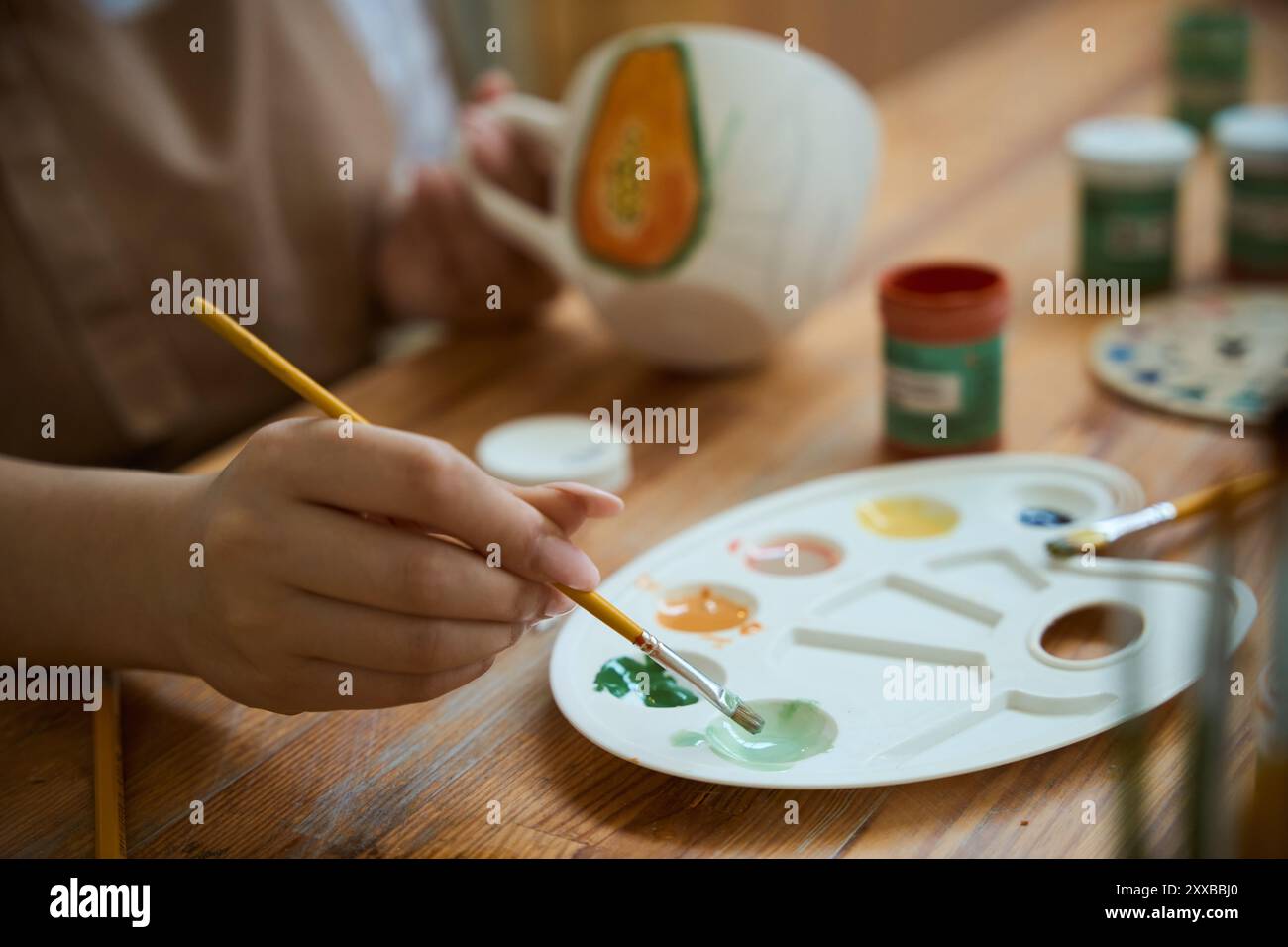 Female hand dipping paintbrush into palette while painting on clay ...