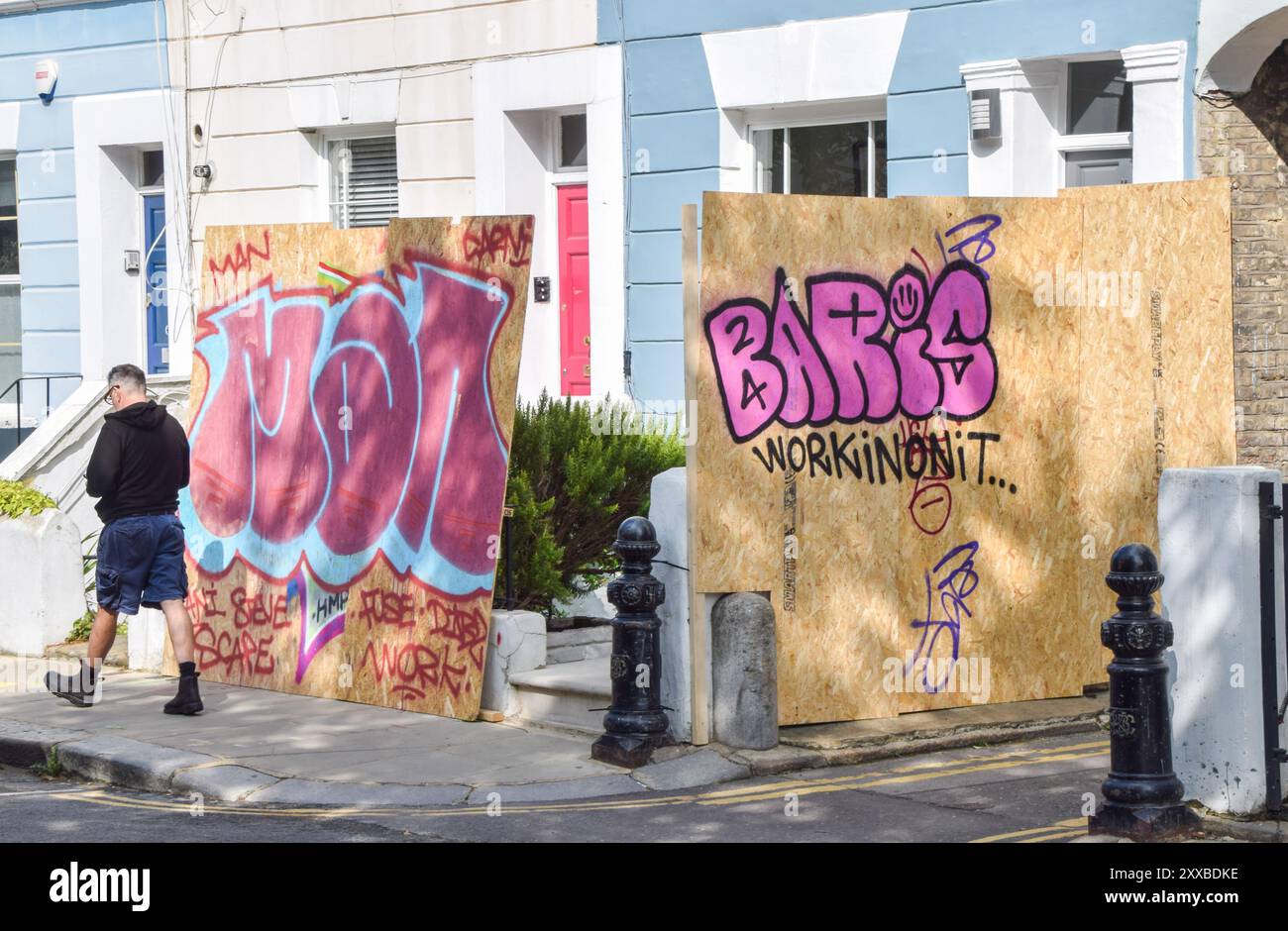 A man walks past protective boards covered in graffiti outside a ...