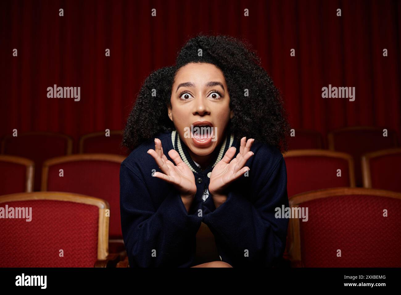 A black woman in casual clothes sits in a movie theater, hands raised ...