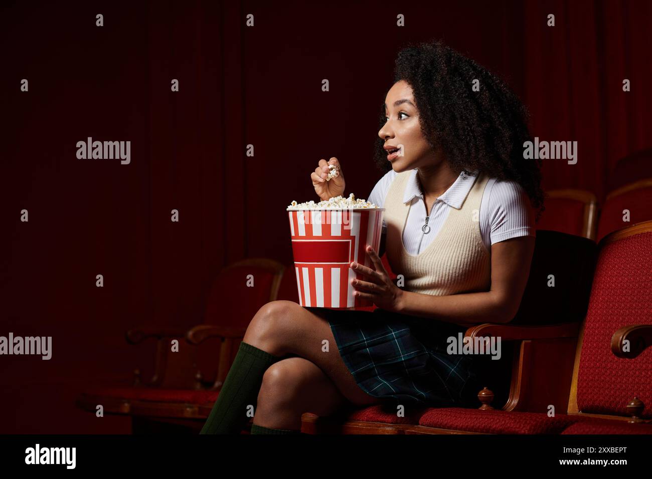 A young woman captivated by the film on screen, sits in a theater seat ...