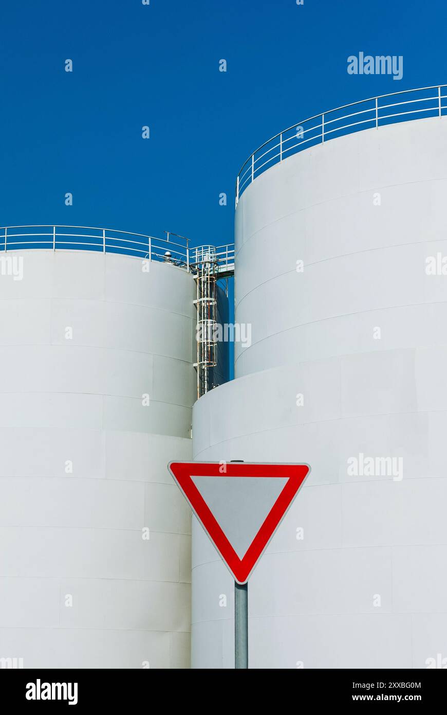 Give way traffic sign in front of white oil tank plants Stock Photo - Alamy
