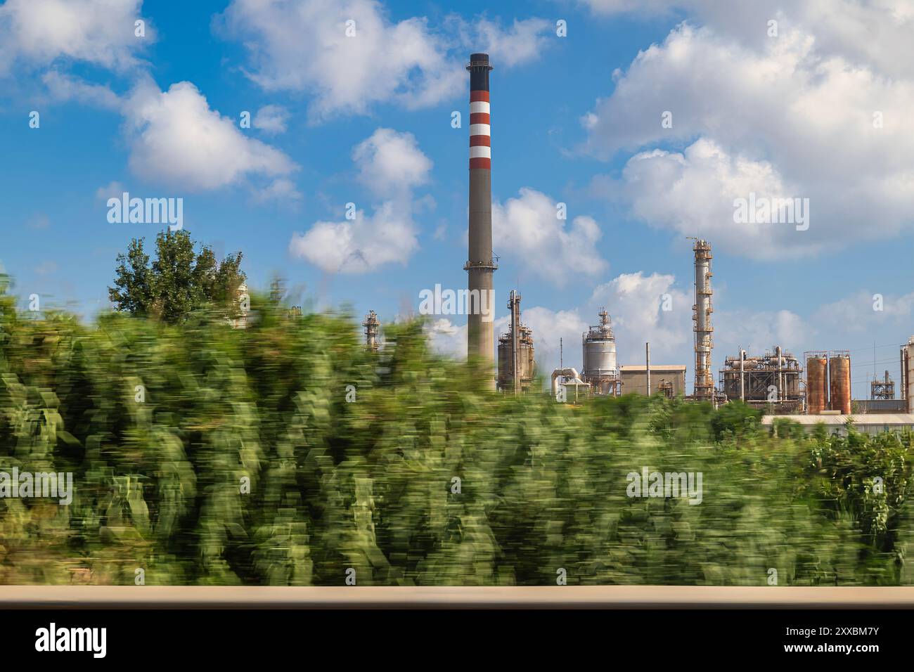 Snapshot taken from a car of an oil refinery amidst vegetation and a ...
