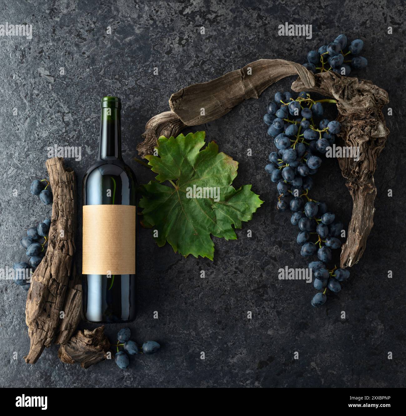 Bottle of red wine, blue grapes, and old vine snags on a black stone ...
