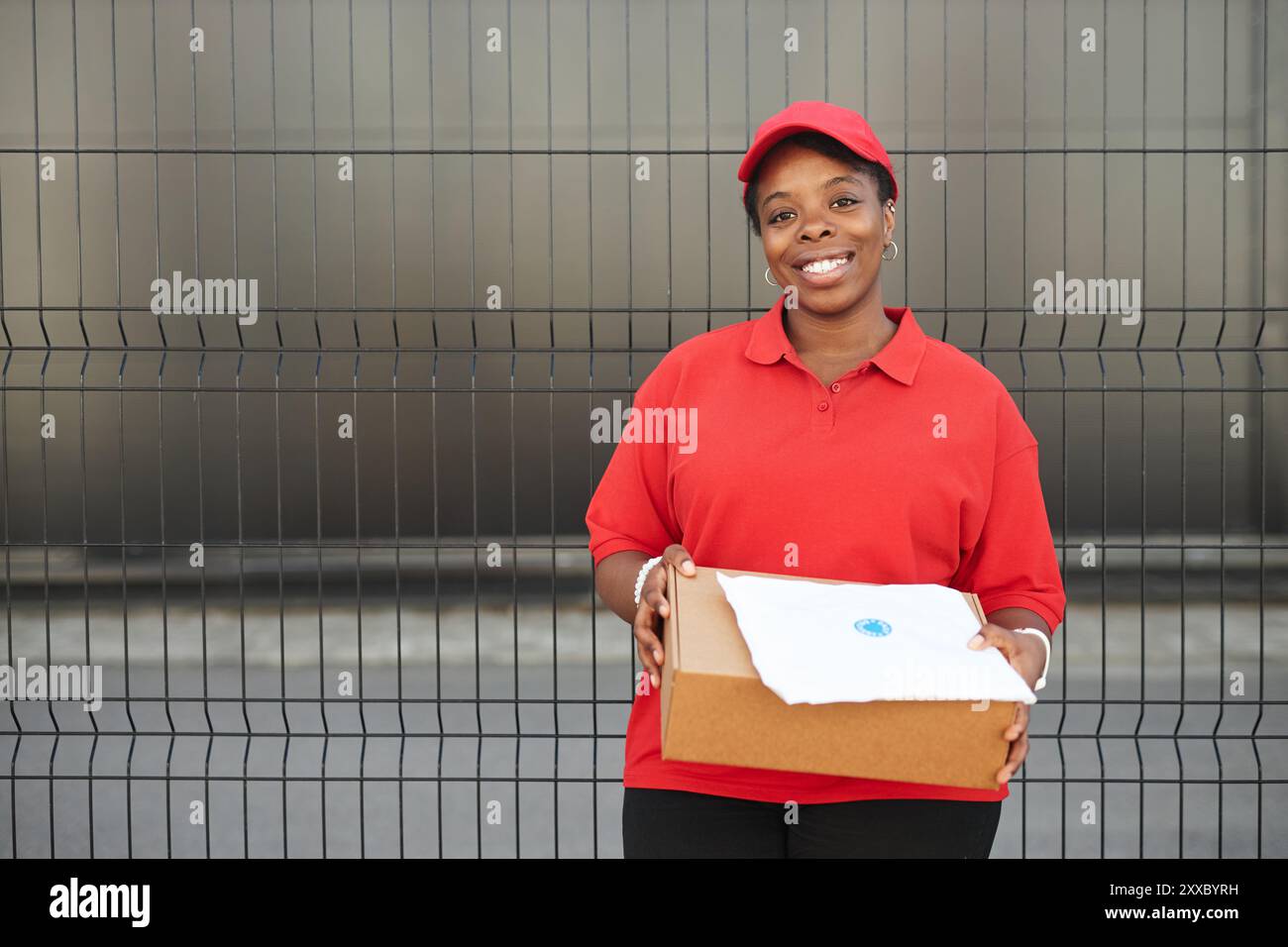 Delivery worker smiling while holding brown package in front of metal ...