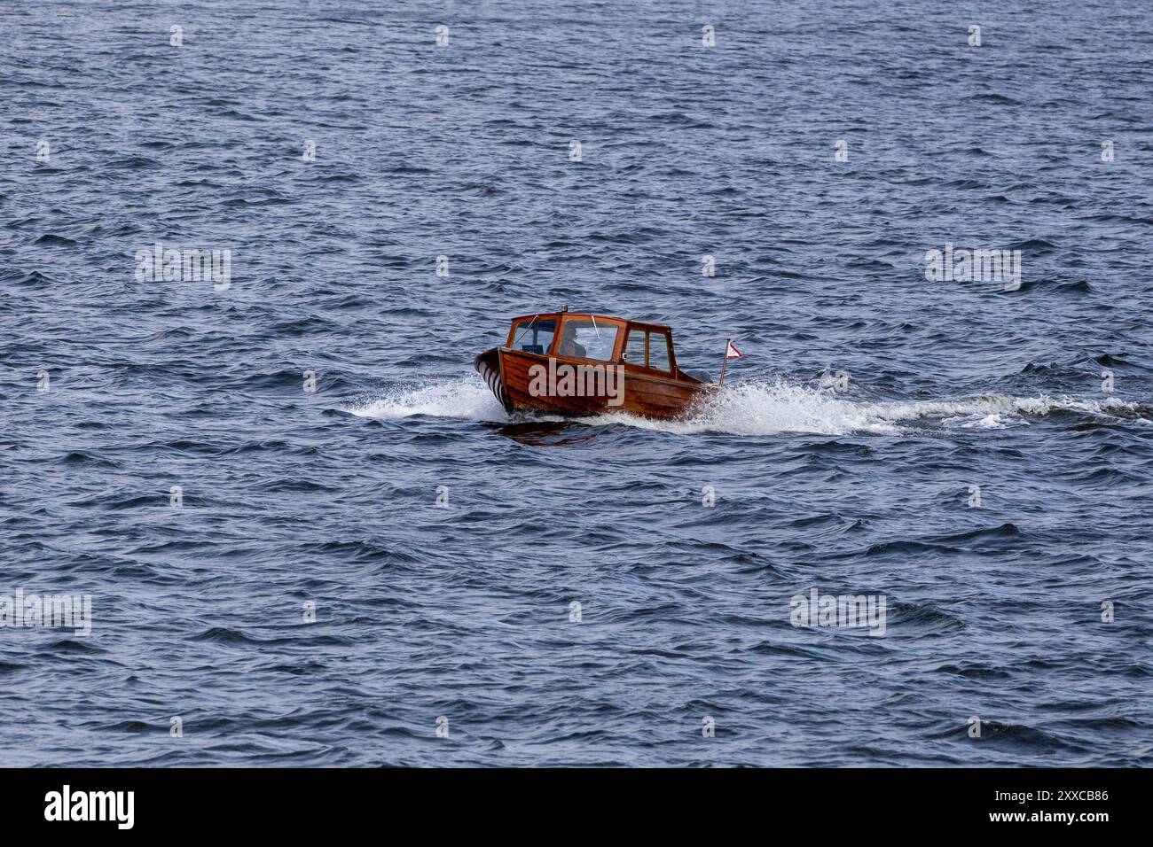 A wooden boat cruising on a calm body of water, creating small waves as ...