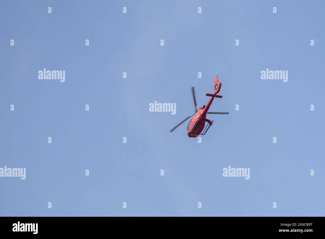 A red helicopter flying in a clear blue sky, showcasing its rotors in ...