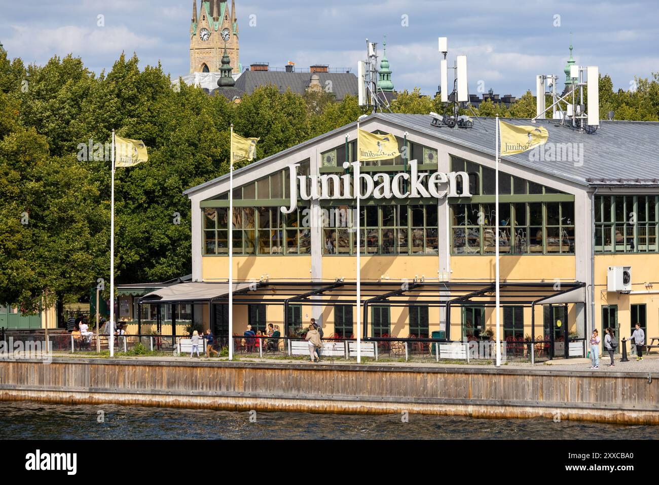 A vibrant building named Junibacken located by a waterfront, surrounded by lush green trees. The ...