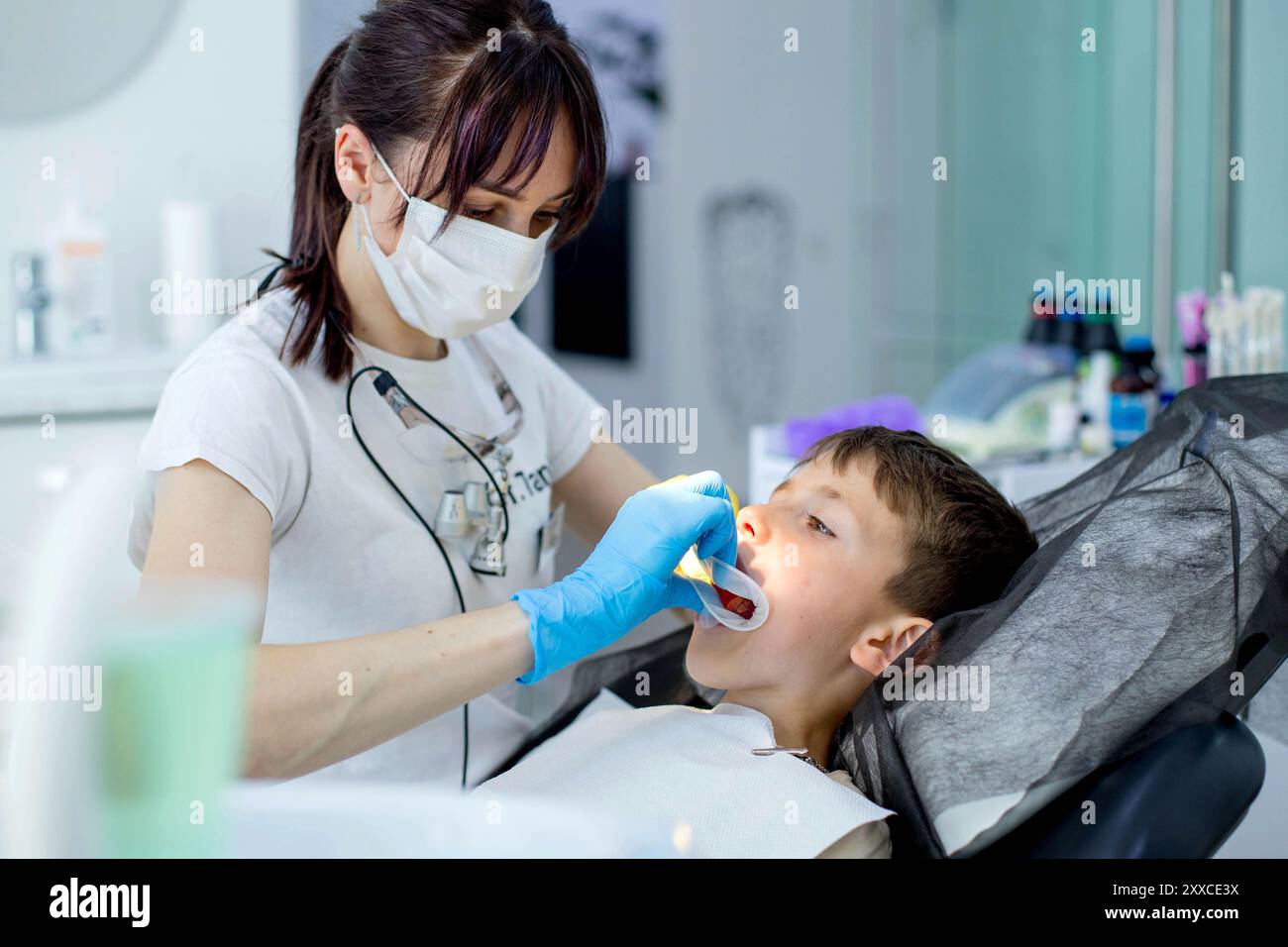 Paediatric dentist putting a cheek retractor on child patient before ...