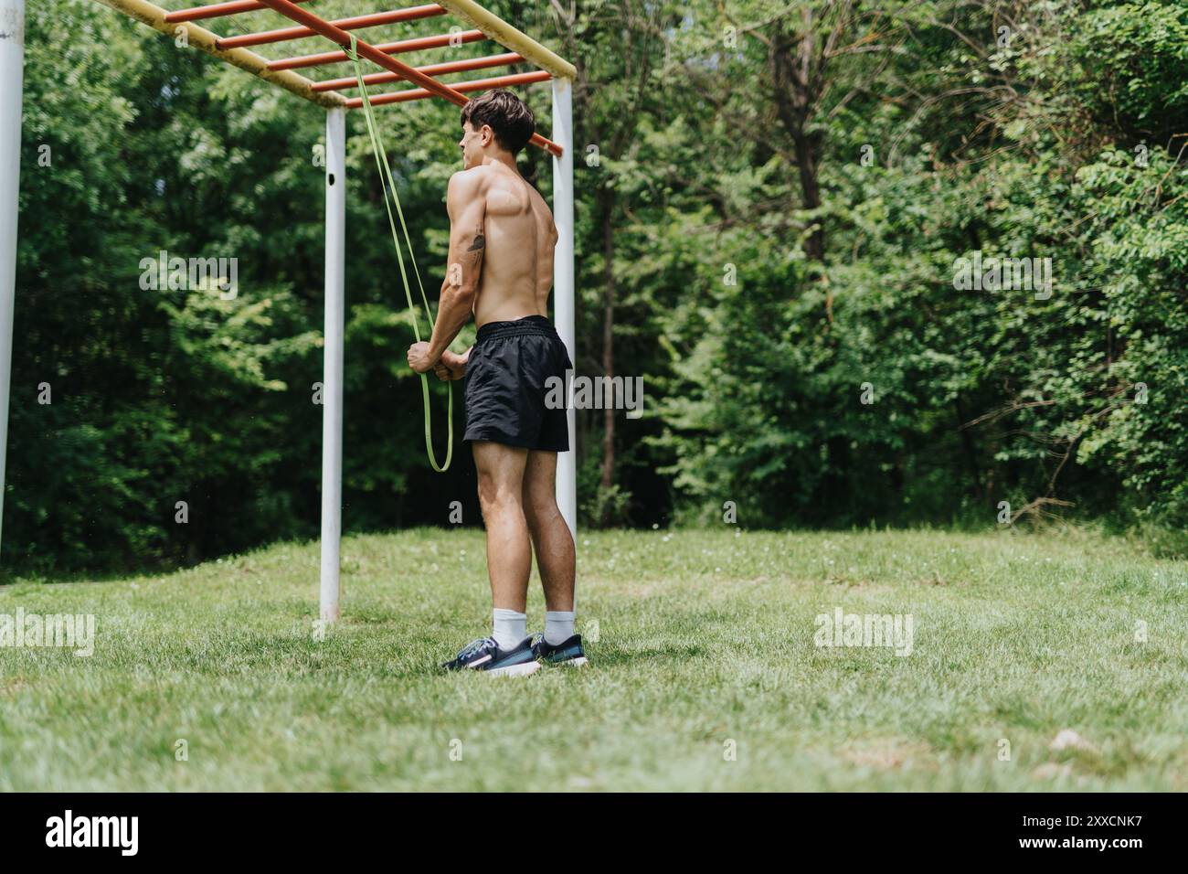 Fit man exercising in nature using monkey bars and resistance band in ...