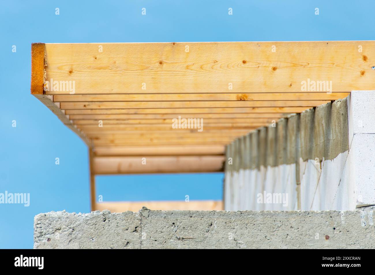 Wooden roof trusses extend over a concrete wall, offering structural ...