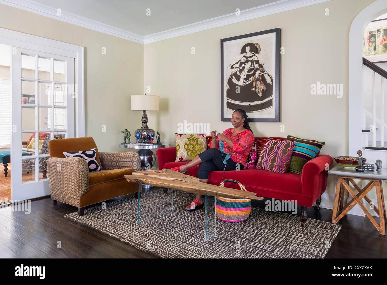 Woman knitting on bright red velvet sofa in her colorful living room ...