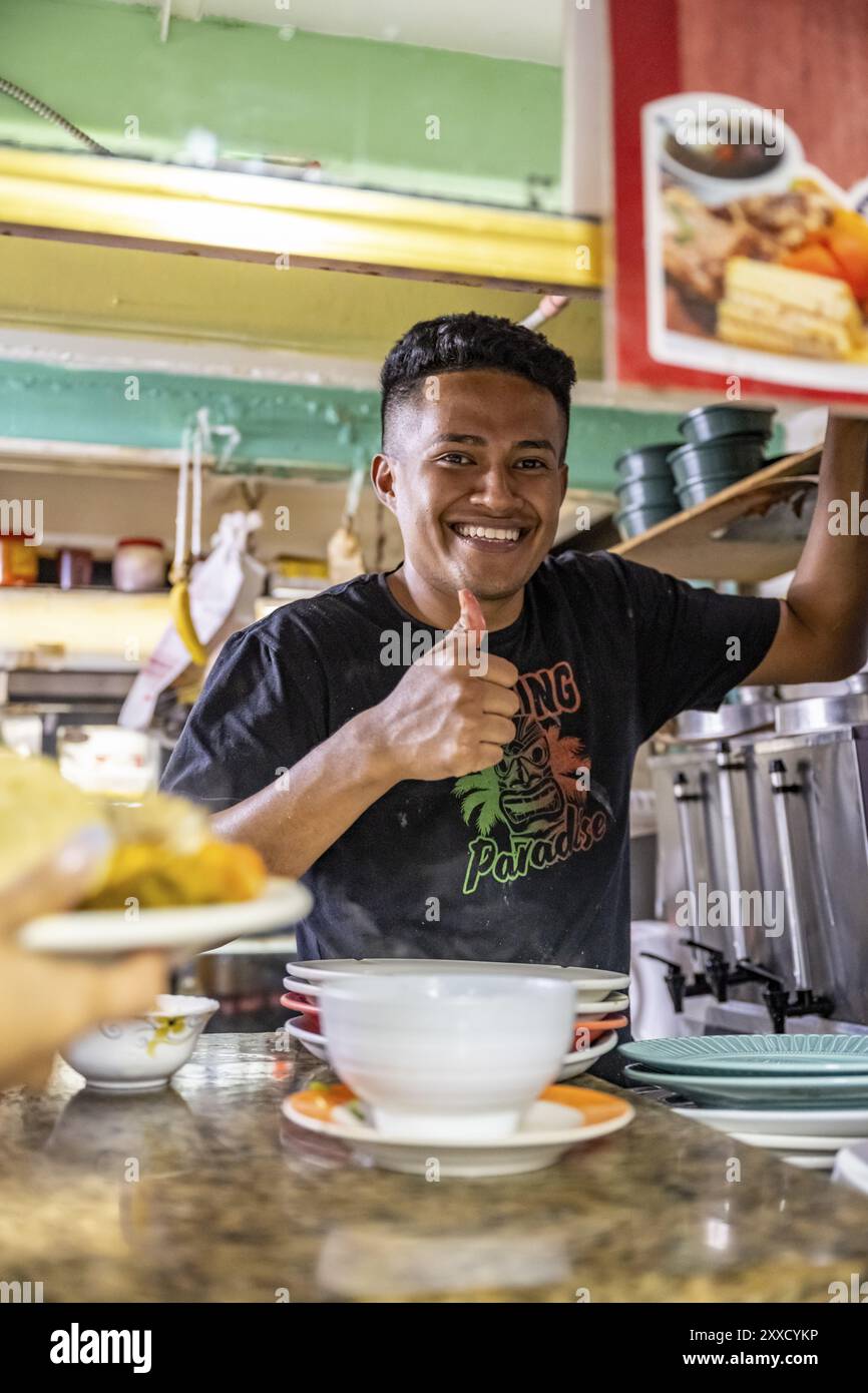Vendor at a food stall shows thumbs up, looks into the camera, Mercado Central de San Jose, San ...