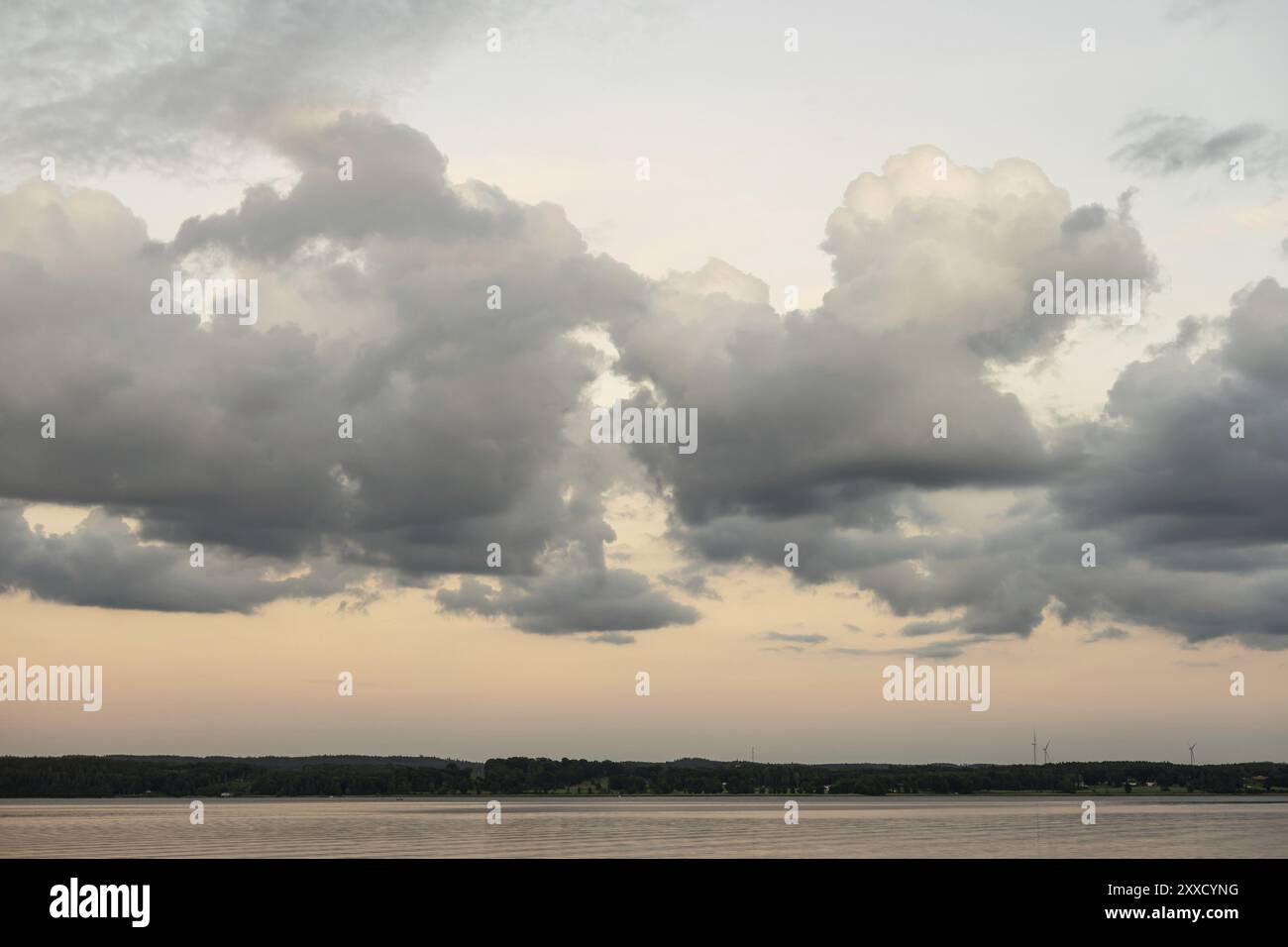 Mighty clouds over a lake shoreline with wind turbines on the horizon ...