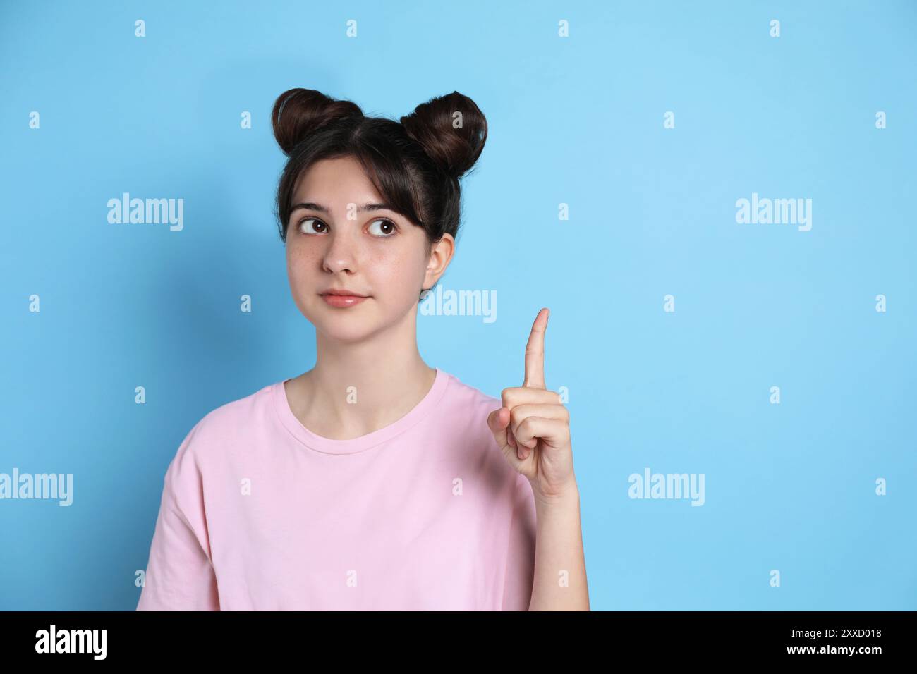 Portrait of cute teenage girl pointing at something on light blue ...