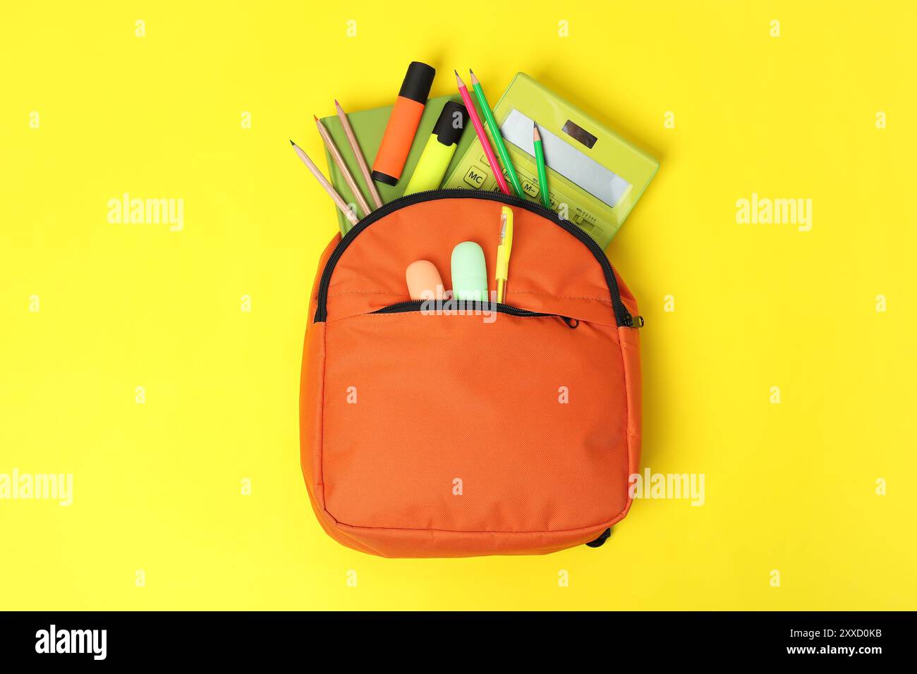 Orange backpack and different school supplies on yellow background, top ...