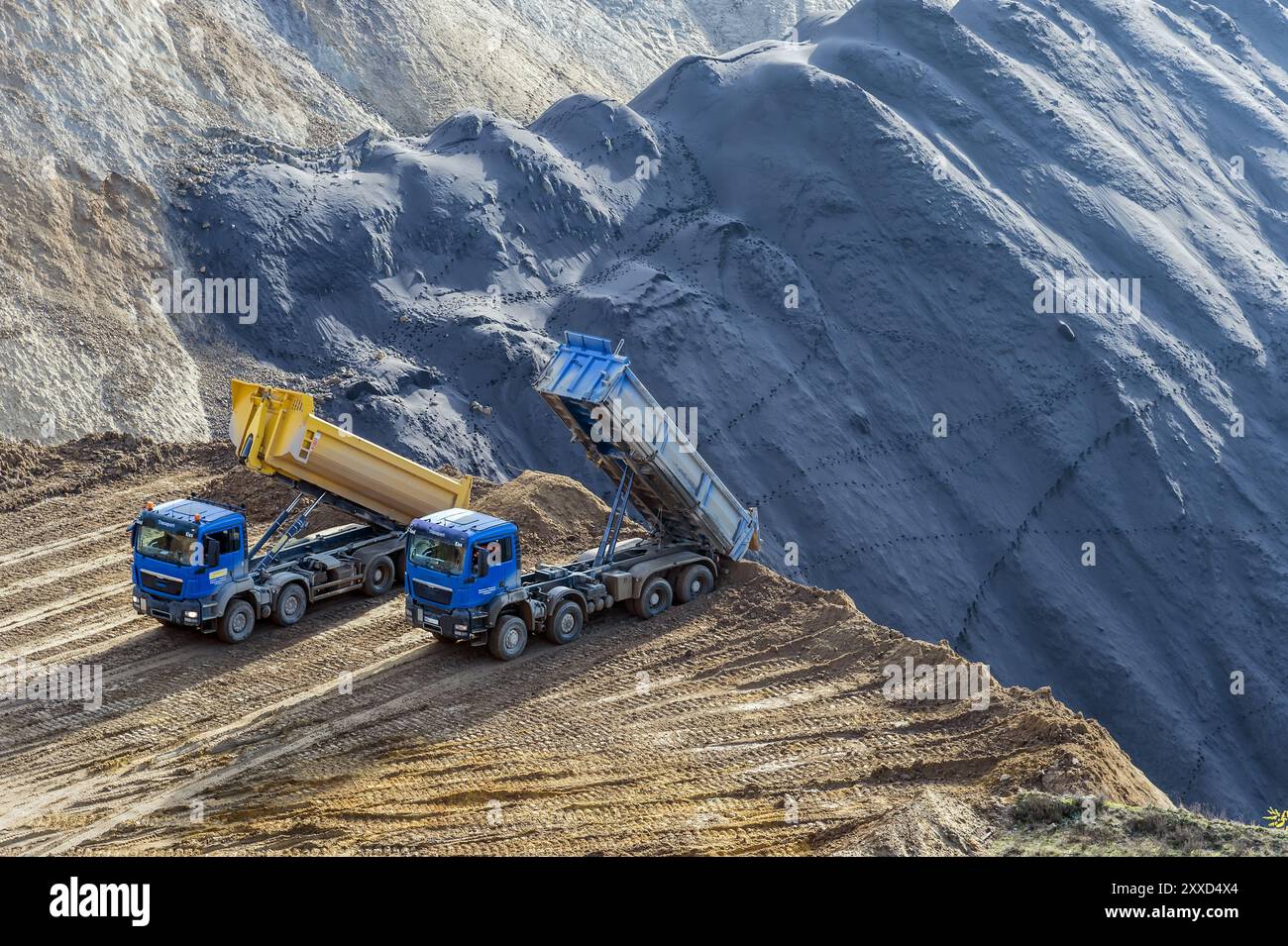 2 dumper trucks stand at the edge of the open-cast mine and tip over a ...