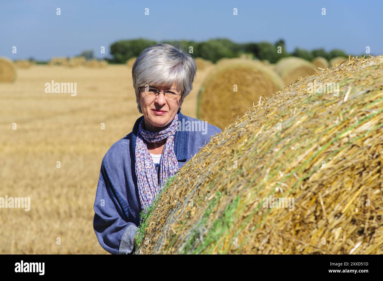 Elderly lady standing behind a bale of straw Stock Photo - Alamy
