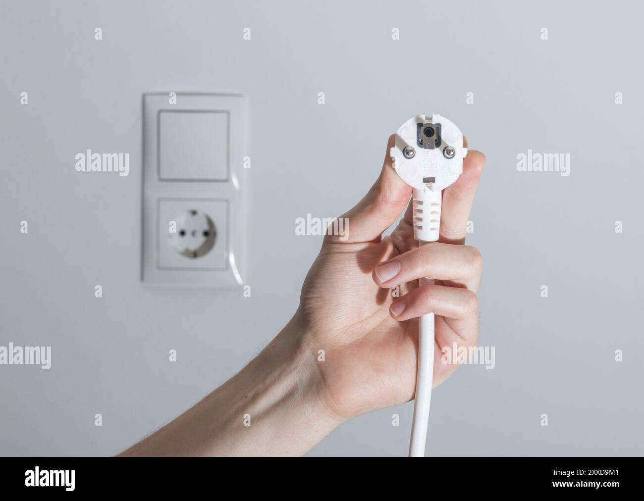White plug with cable in males hand, ready to connect. Energy concept ...